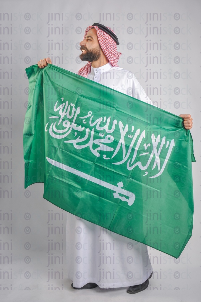 A Saudi man smiling and holding the Saudi Arabian flag with his hands ...