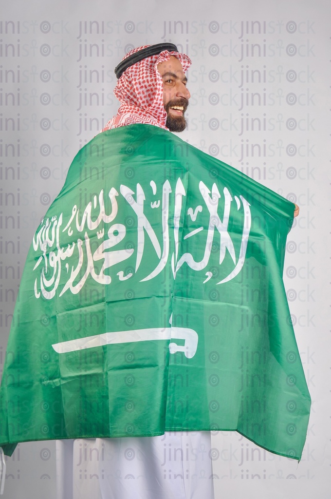 A Saudi man smiling and wearing the Saudi Arabian flag to celebrate the ...