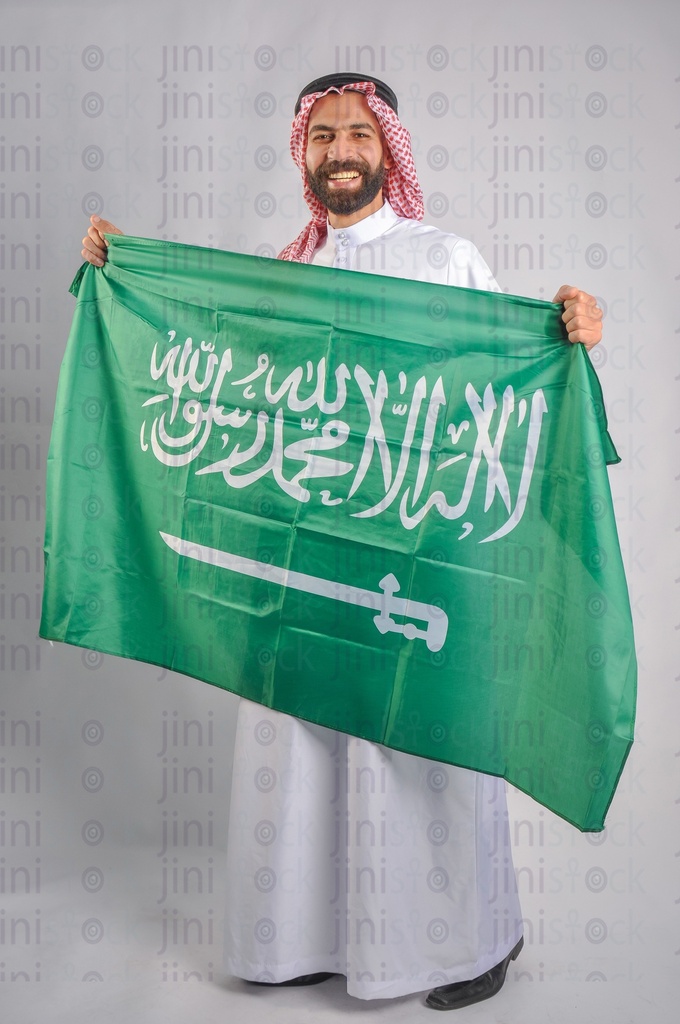 A Saudi man smiling and holding the Saudi Arabian flag with his hands ...