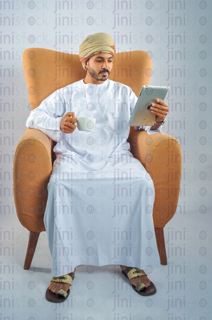 An Omani man wearing Omani uniform working and sitting on a chair ...